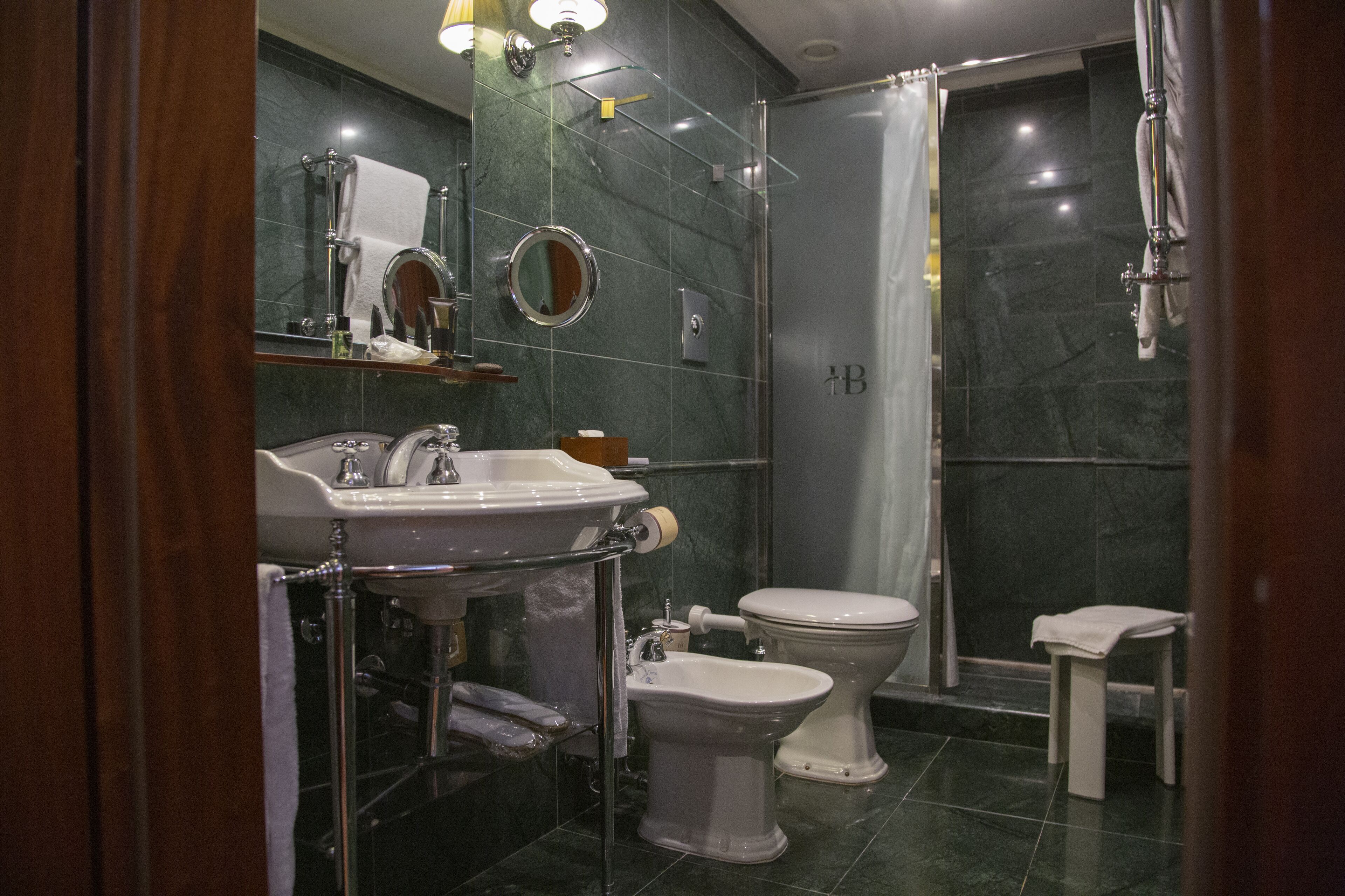 Uma casa de banho moderna com lavatório, duas sanitas, bidé e cabine de duche com parede de vidro.
