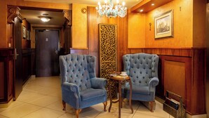 Um saguão com dois poltronas azuis, um aparador de madeira, um candelabro e um quadro emoldurado na parede.