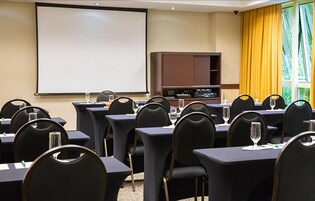 Uma sala de conferências com mesas, cadeiras, uma tela de projetor e um armário.