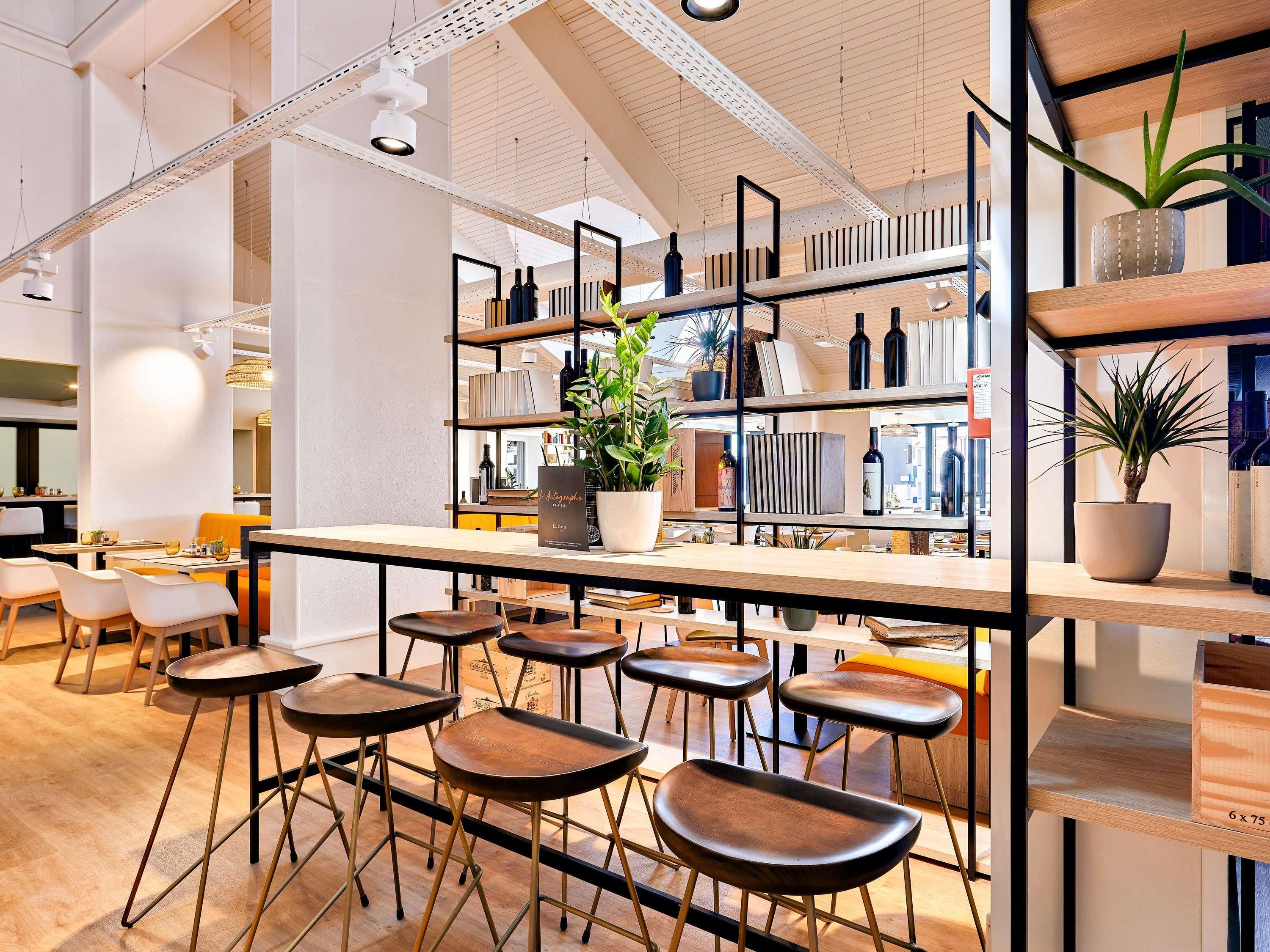 Uma área de bar moderna com banquetas, prateleiras com garrafas e plantas em vasos.