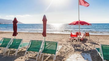 Uma praia com cadeiras de praia verdes e guarda-sóis vermelhos.