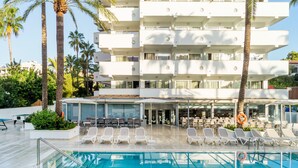 Um hotel moderno com área de piscina, cadeiras de descanso e palmeiras.