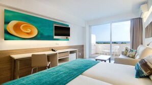 Quarto de hotel com cama, escrivaninha, cadeira, televisão e varanda com vista para o mar.