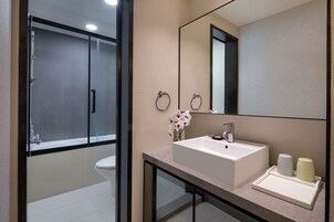 Um banheiro moderno com box de vidro, pia branca e um espelho grande.