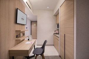 Quarto de hotel moderno com escrivaninha de madeira, cadeira, televisão de tela plana e armários embutidos de madeira.