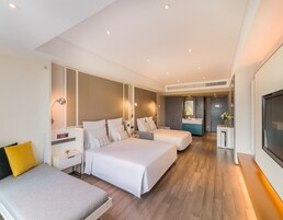 Quarto de hotel moderno com duas camas de solteiro, um sofá-cama, uma pequena mesa de trabalho e uma TV.