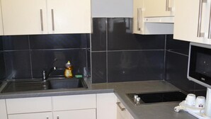 Uma cozinha compacta com armários brancos, uma pia de aço inoxidável e um micro-ondas embutido.