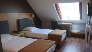 Quarto de hotel com duas camas, uma escrivaninha, uma cadeira e uma janela com cortinas.