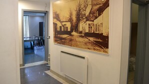 Um corredor com uma grande fotografia histórica na parede, um radiador e uma porta que dá para um quarto com mesa e cadeiras.