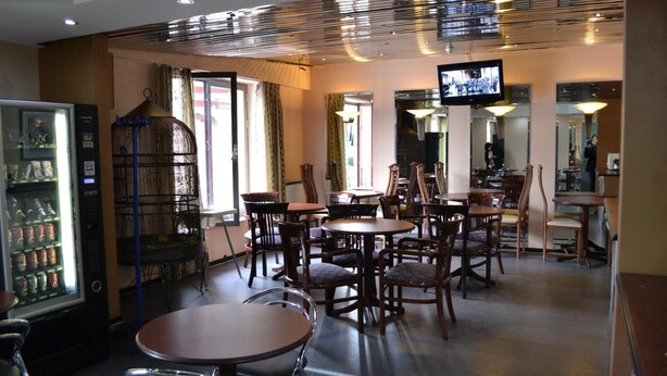 Um restaurante com mesas e cadeiras redondas, uma máquina de vendas automática e uma tela de televisão.