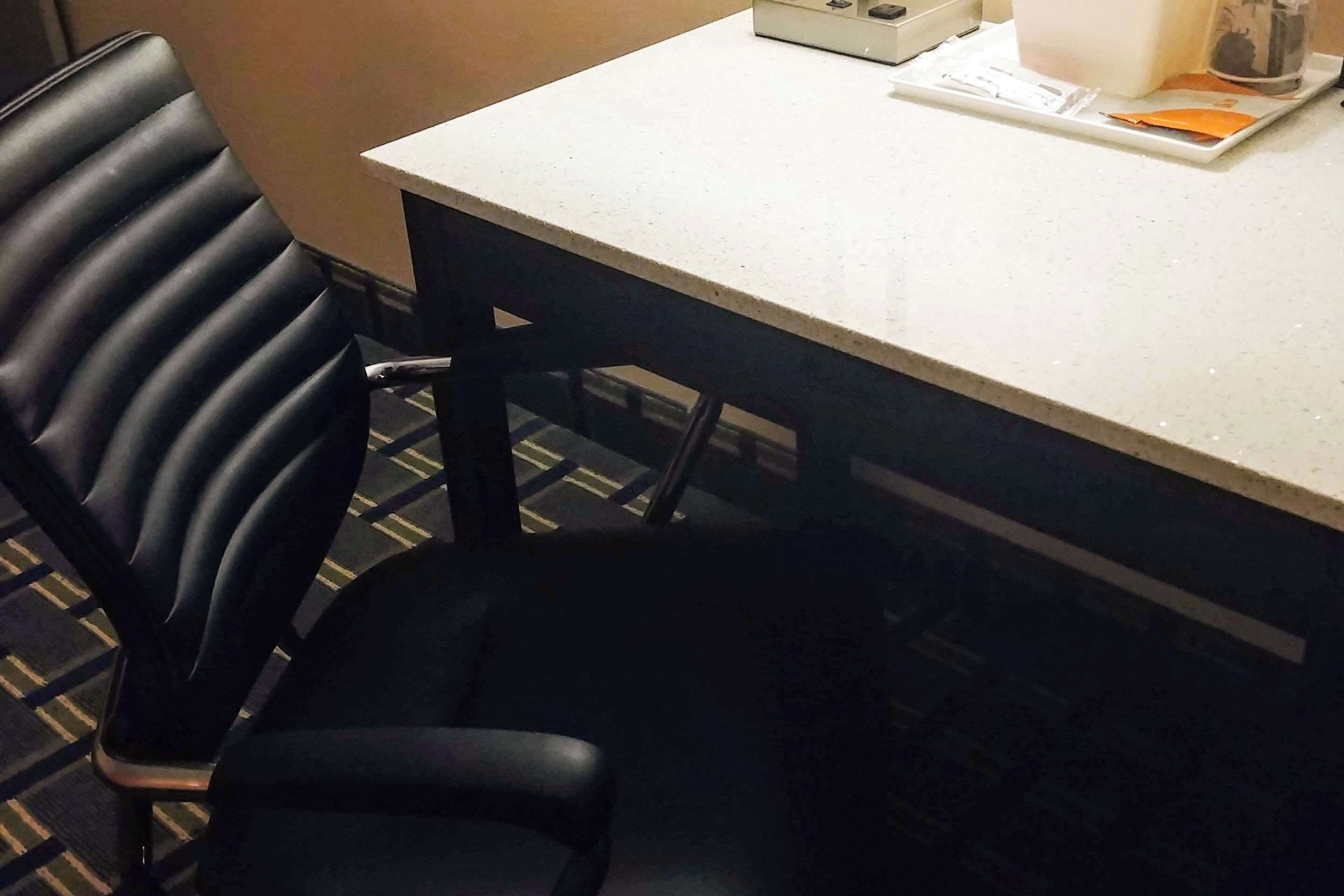 Quarto de hotel com uma mesa branca, cadeiras pretas e um chão estampado.