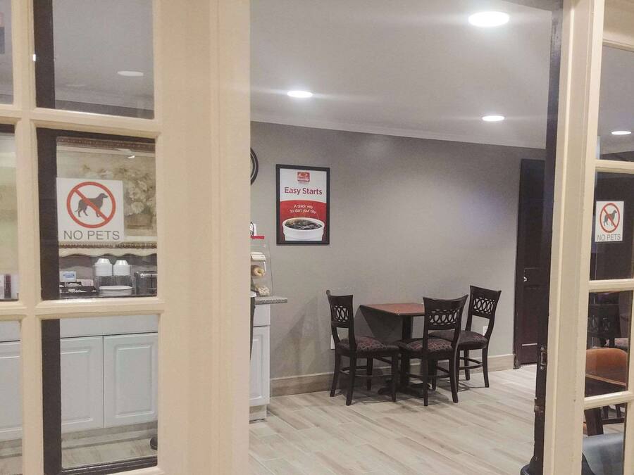 Uma área de refeições com uma mesa e cadeiras, e um aviso 'NÃO PERMITIDOS ANIMAIS' na janela.