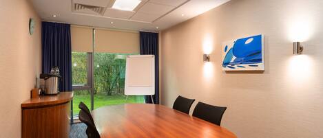 Sala de conferência com mesa de madeira, cadeiras, um quadro branco e vista para o verde lá fora.