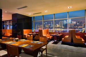 Restaurante com vista para o horizonte urbano, mobiliário moderno e uma mesa grande posta para convidados.