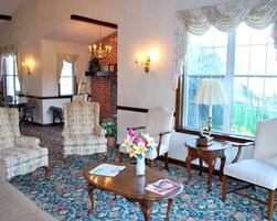 Quarto com carpete estampado, poltronas florais, mesa de centro de madeira com uma revista, um vaso com flores e vista para o verde através de uma janela.