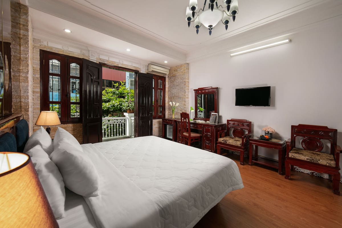 Quarto de hotel com cama grande, móveis de madeira, televisão e varanda com plantas.