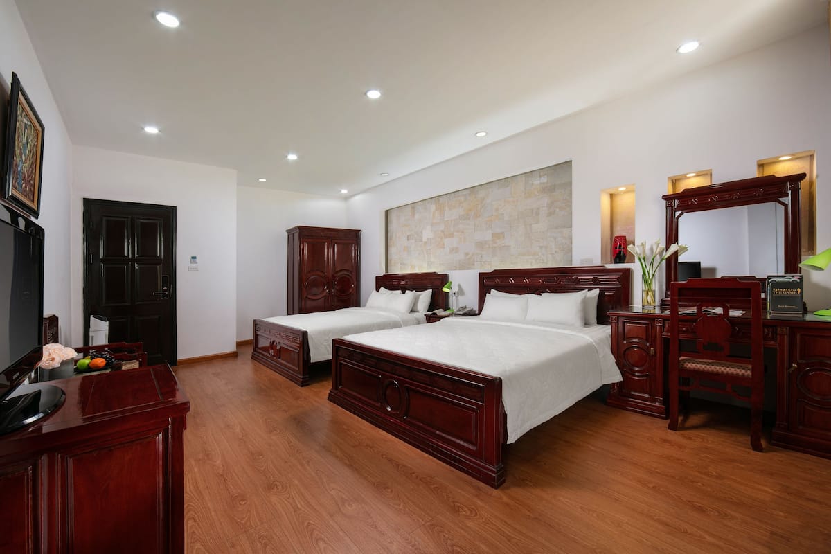 Quarto de hotel com duas camas de madeira, uma escrivaninha, uma cadeira e um espelho grande.