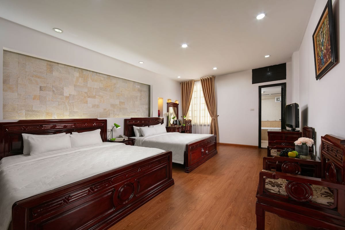 Quarto de hotel com duas camas de madeira, uma grande parede de pedra, uma televisão de tela plana e um aparador de madeira.
