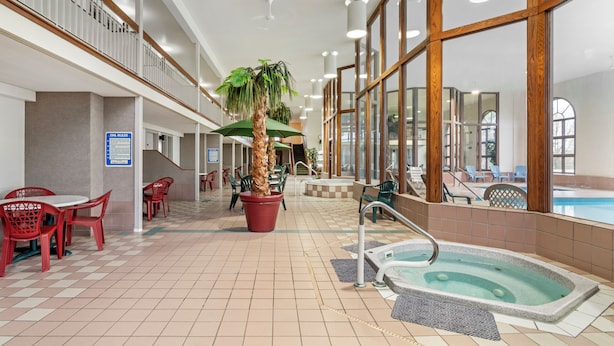 Uma área de piscina interna com hidromassagem, cadeiras vermelhas e uma palmeira.