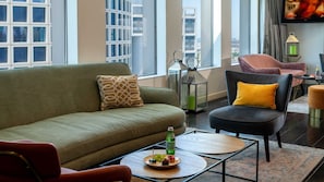 Uma sala moderna com um sofá verde, uma poltrona preta e uma mesa de centro com petiscos.