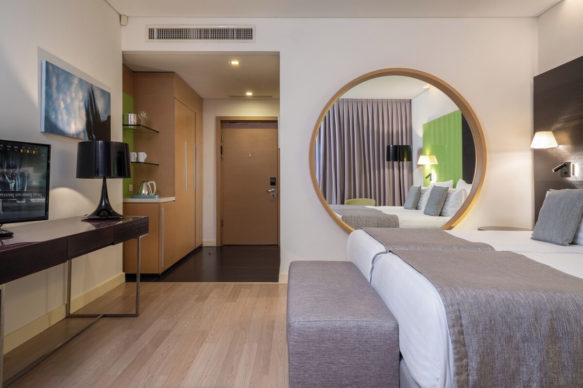 Quarto de hotel moderno com uma cama, uma mesa com computador, um espelho e vista do quarto através de um espelho circular.