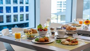 Mesa de café da manhã com diversos pratos, incluindo waffles, croquetes e uma salada, acompanhados de bebidas e uma xícara de café.