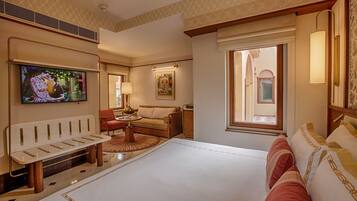 Quarto de hotel com uma cama grande, televisão, sofá, mesa pequena e janela com vista para o exterior.
