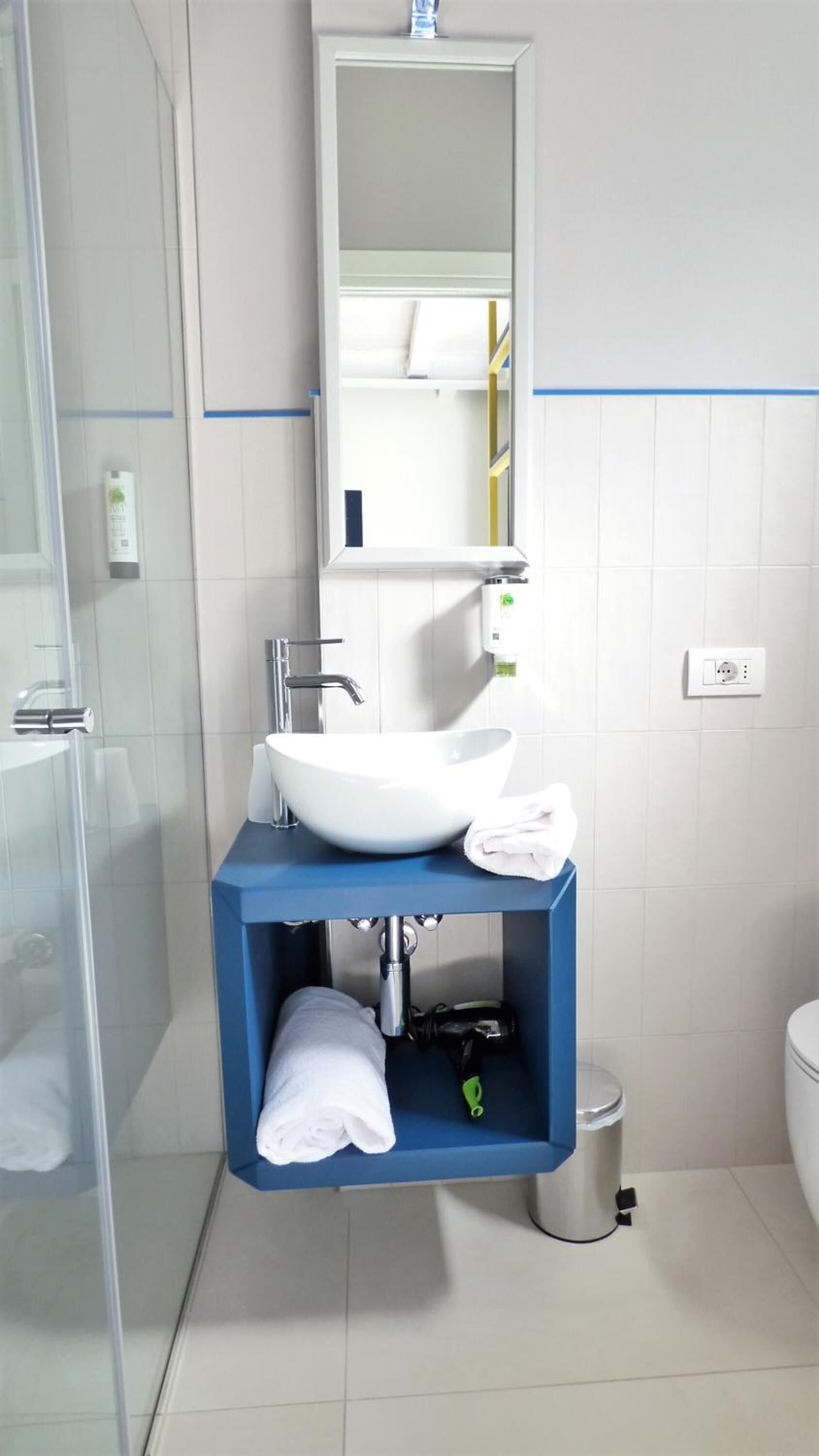 Casa de banho com lavatório branco, toucador azul e cabine de duche em vidro.
