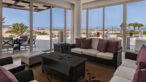 Uma sala de estar espaçosa com uma grande porta de vidro que dá para uma varanda com vista para a praia.