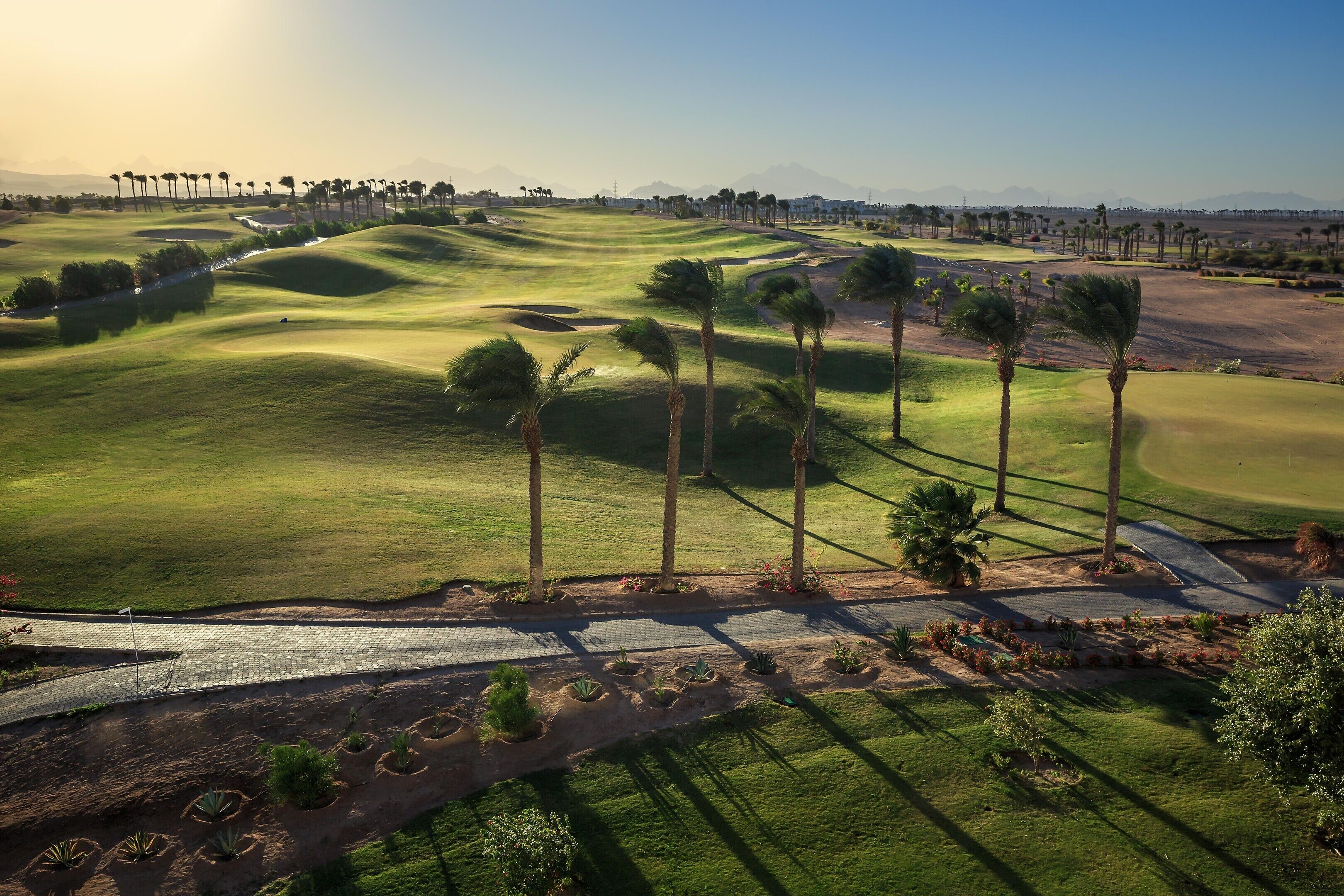 Um campo de golfe com fairways bem cuidados, bunkers de areia e vista desobstruída para montanhas ao longe.