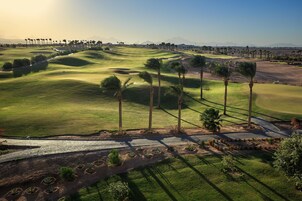 Um campo de golfe com fairways bem cuidados, bunkers de areia e vista desobstruída para montanhas ao longe.