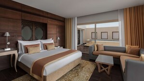 Quarto de hotel com uma cama grande, um sofá, uma mesinha e vista para o exterior.