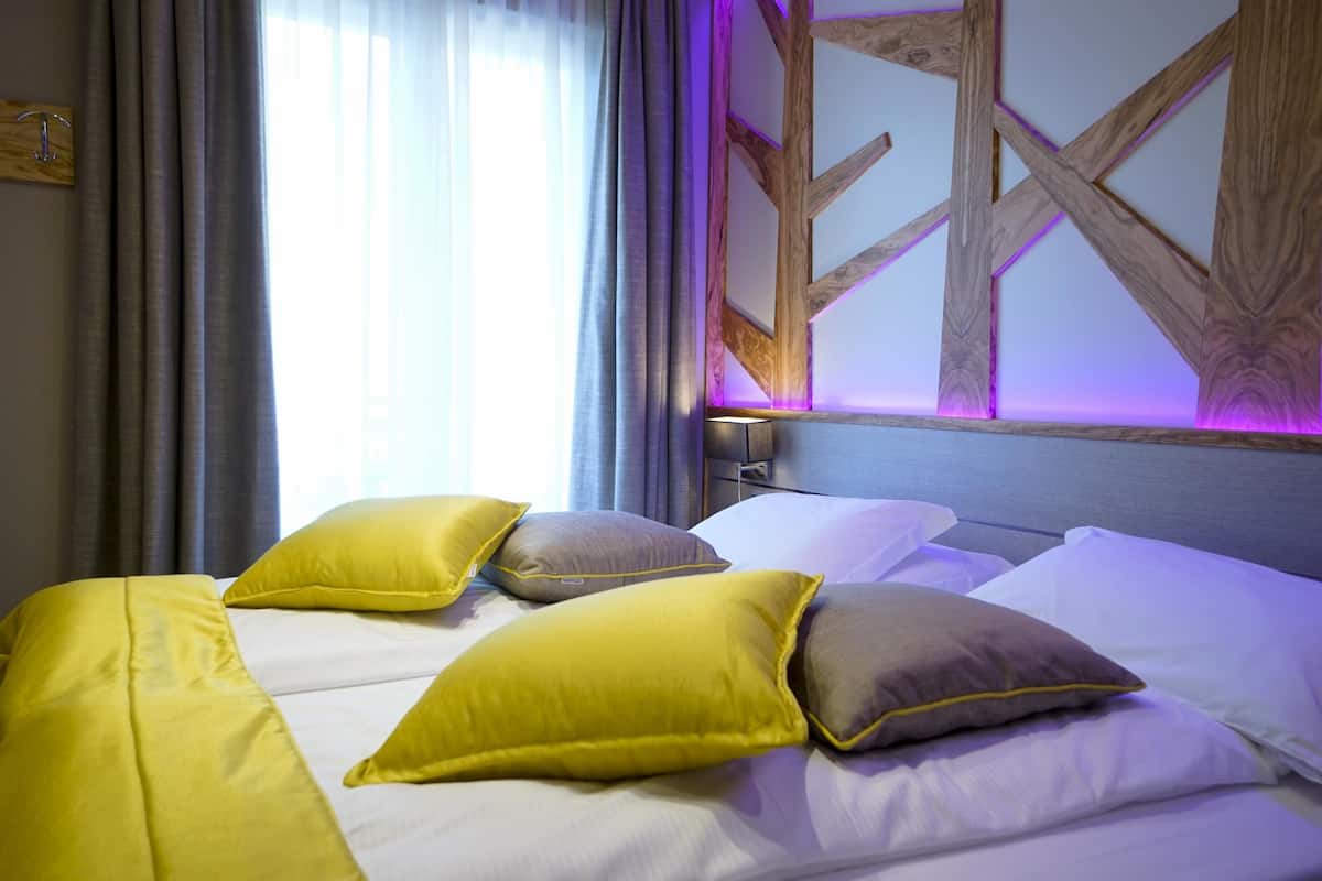 Quarto de hotel com cama, almofadas, cortinas e uma parede com design geométrico.