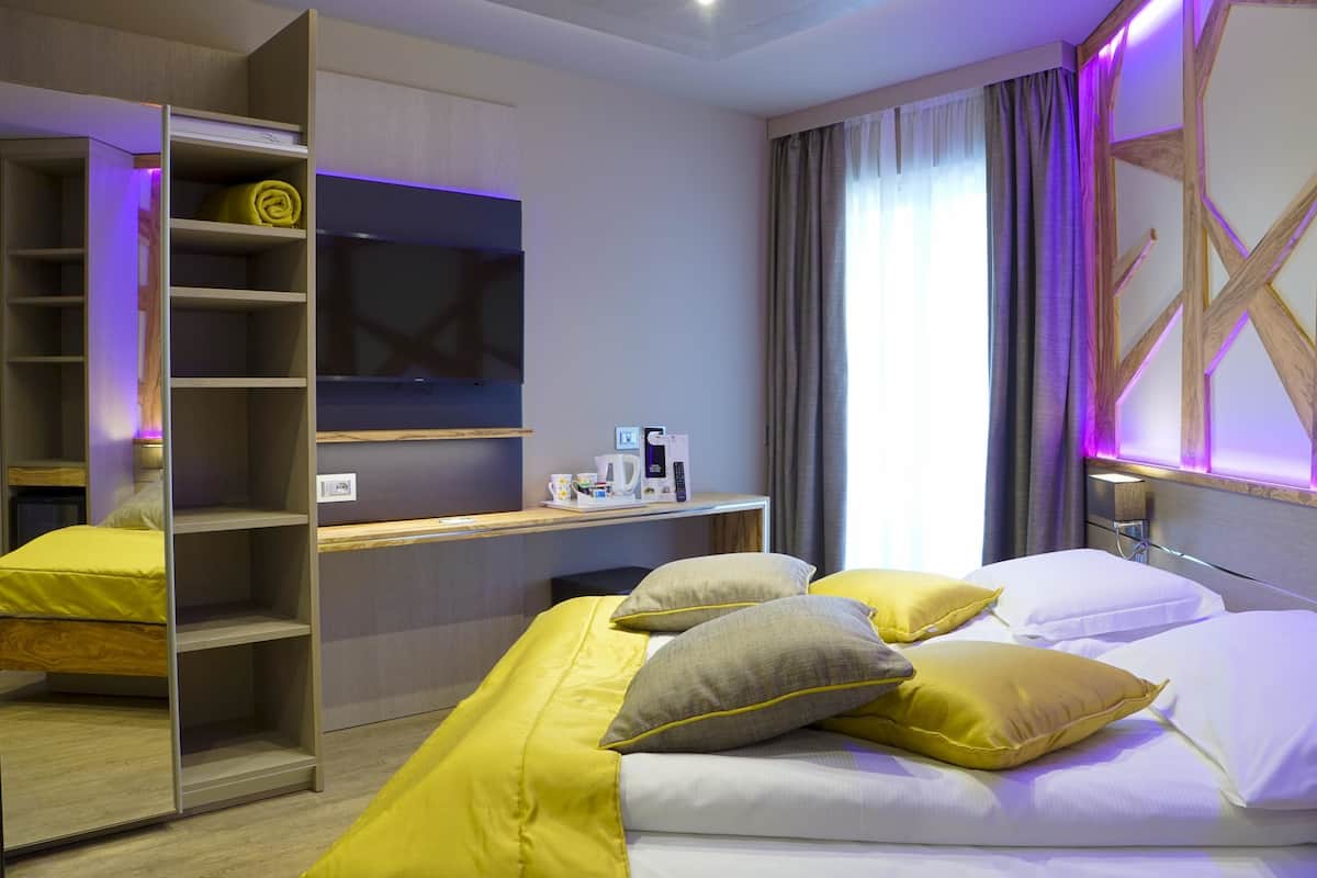 Quarto de hotel moderno com uma cama, uma televisão, uma escrivaninha e um guarda-roupa.