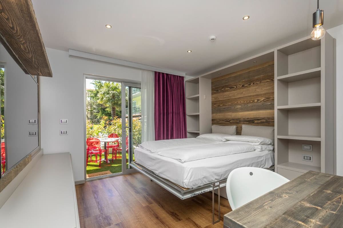 Quarto moderno com cama, escrivaninha e vista para um jardim.