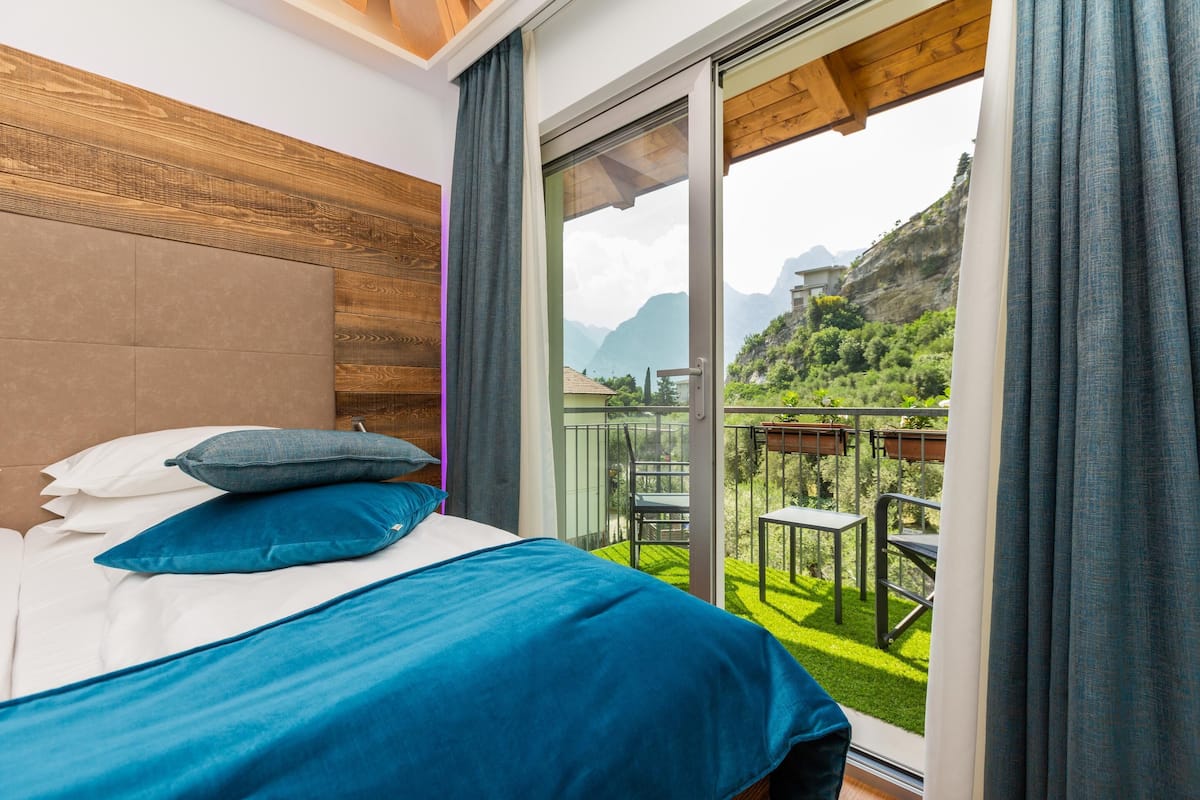 Quarto com uma cama grande, cabeceira de madeira e varanda com mesa e cadeiras.