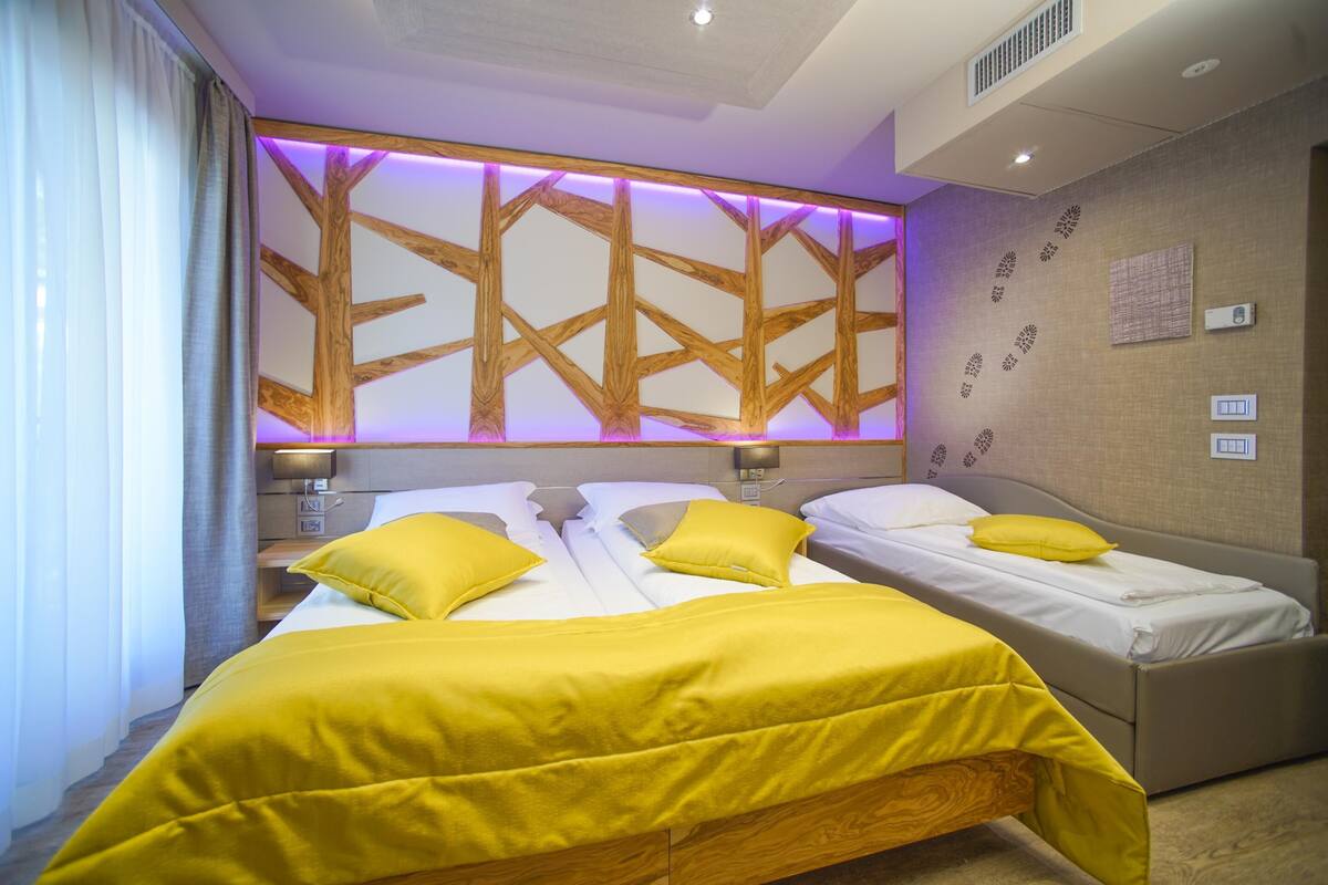 Quarto de hotel com duas camas, cada uma com colcha amarela, uma grande obra de arte na parede e teto com design de vigas de madeira.