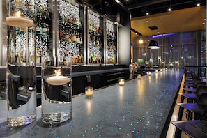 Uma área de bar com um balcão longo, diversas garrafas de álcool e velas.