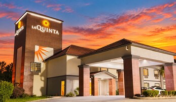 Entrada de hotel com placa visível, estacionamento coberto e céu claro.