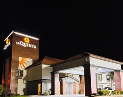 Um hotel com um letreiro chamativo da 'La Quinta', uma entrada coberta e um carro estacionado na frente.
