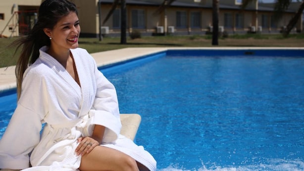 Uma pessoa sentada à beira da piscina, com um edifício ao fundo.