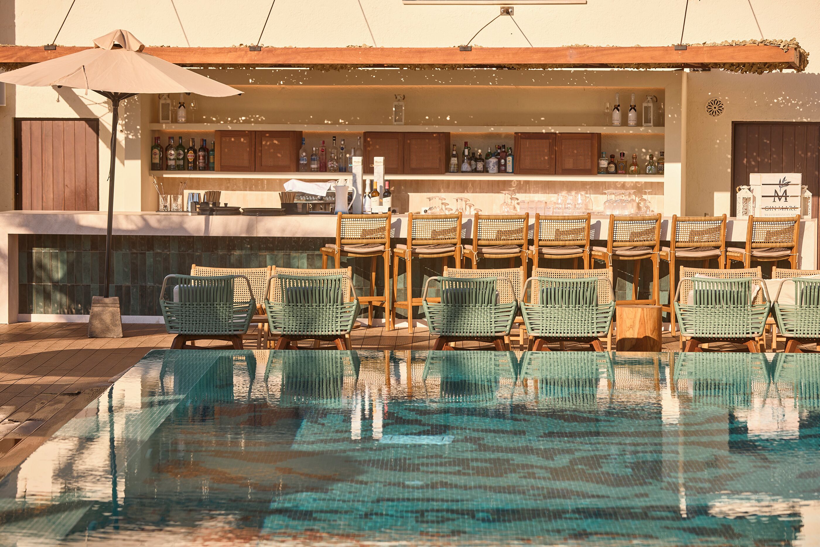 Uma área à beira da piscina com bar, cadeiras de vime e espreguiçadeira.