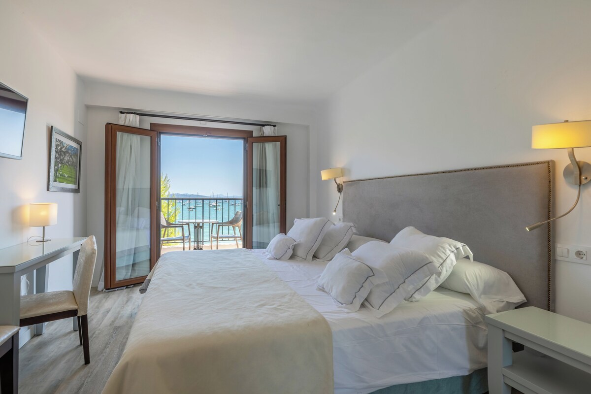 Quarto de hotel com uma cama grande, uma escrivaninha, uma cadeira e varanda com vista.