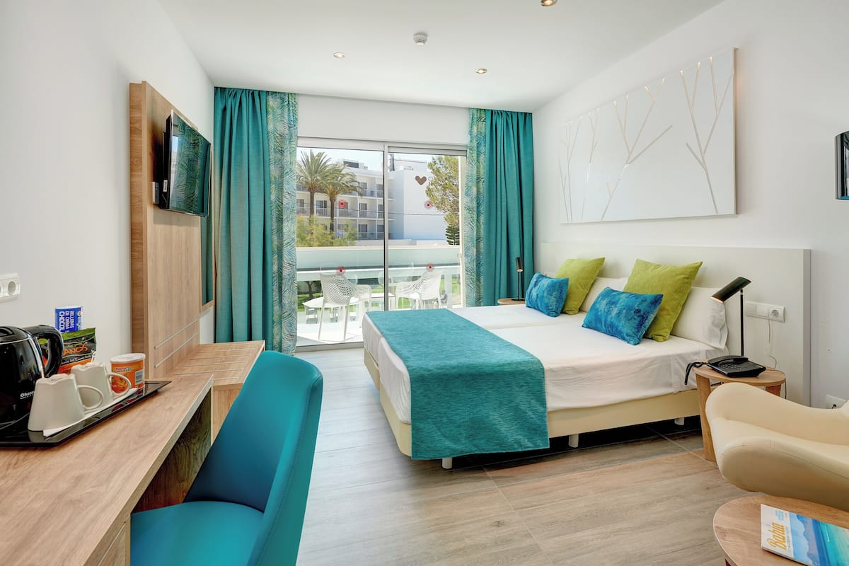Quarto de hotel com cama, escrivaninha, cadeira, televisão e varanda com vista.