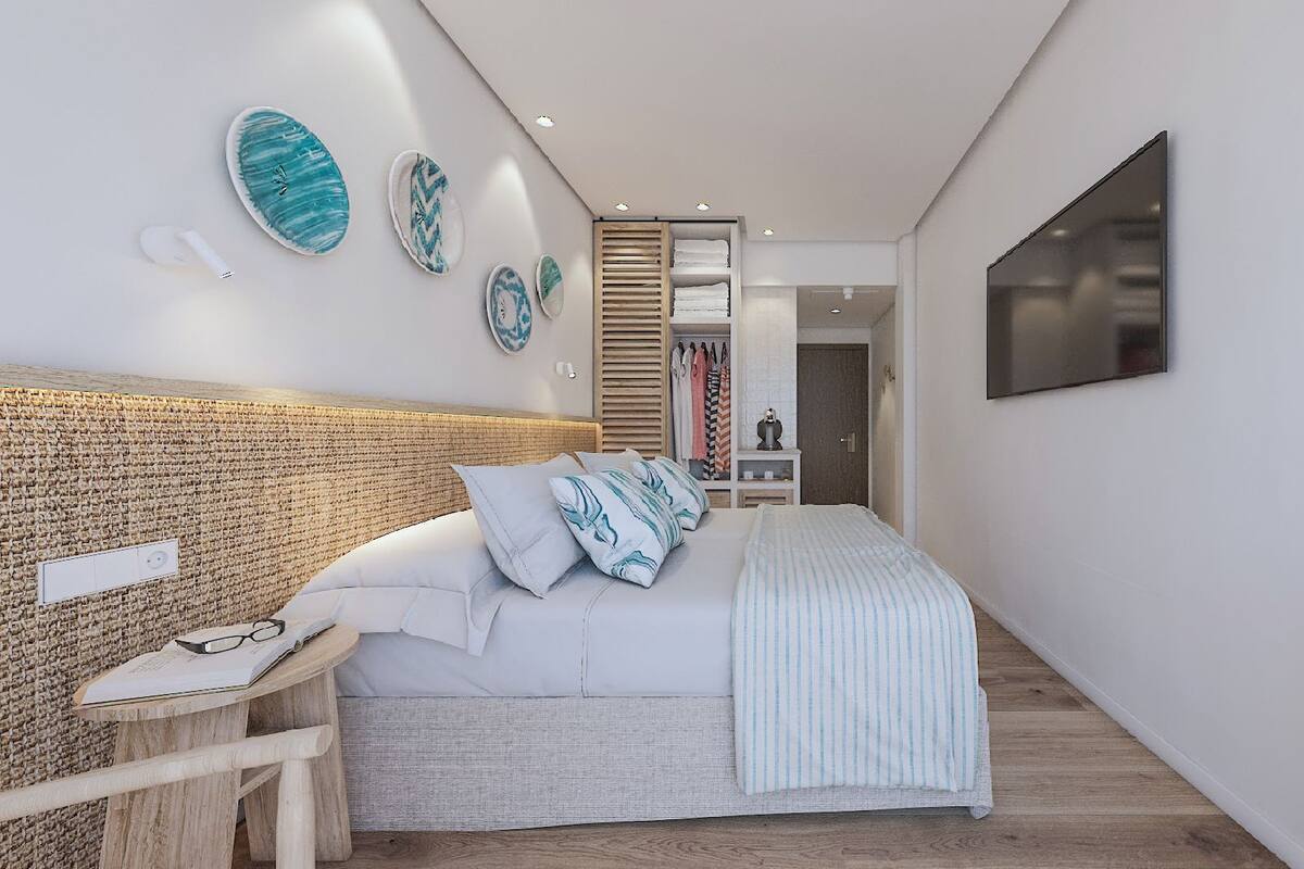 Quarto moderno com cabeceira de tecido trançado, cama com roupa de cama listrada, mesa de cabeceira com copos e um livro, e TV montada na parede.