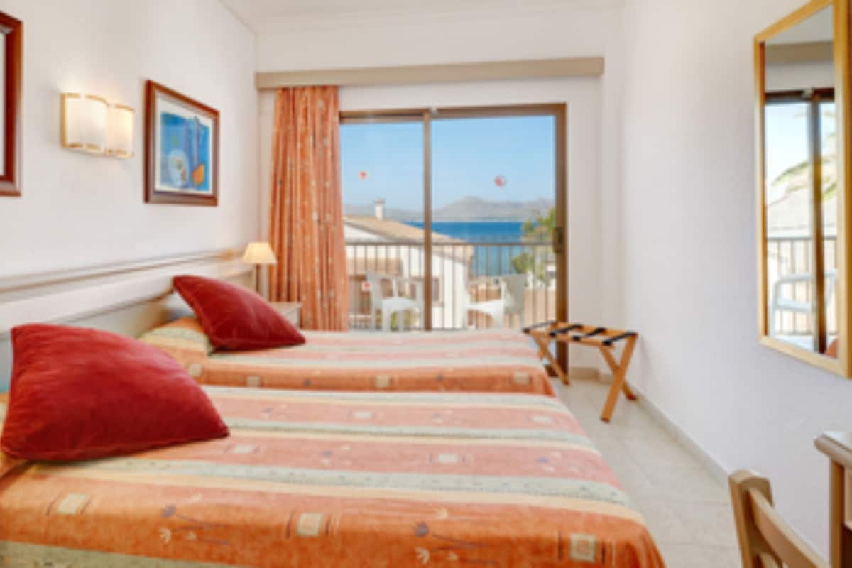 Quarto de hotel com duas camas, varanda com vista, escrivaninha e uma cadeira.