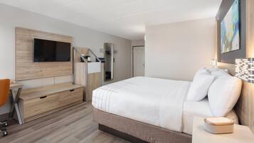 Quarto de hotel moderno com uma cama grande, uma escrivaninha com cadeira, uma TV fixada na parede e uma pequena mesa de cabeceira com abajur.