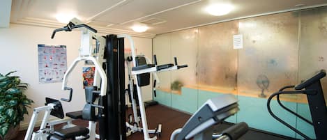 Academia com equipamentos de exercício, esteira e parede com um pôster.