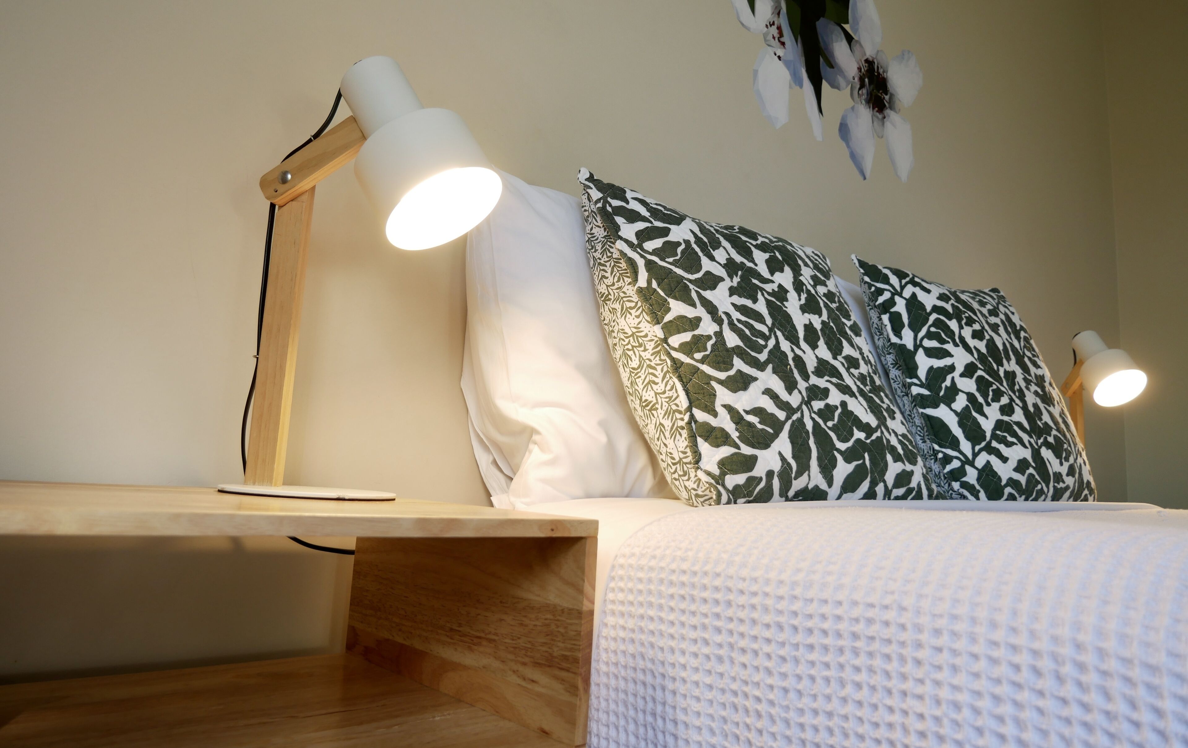 Cama bem arrumada com almofadas estampadas, mesa de cabeceira de madeira e duas luminárias.
