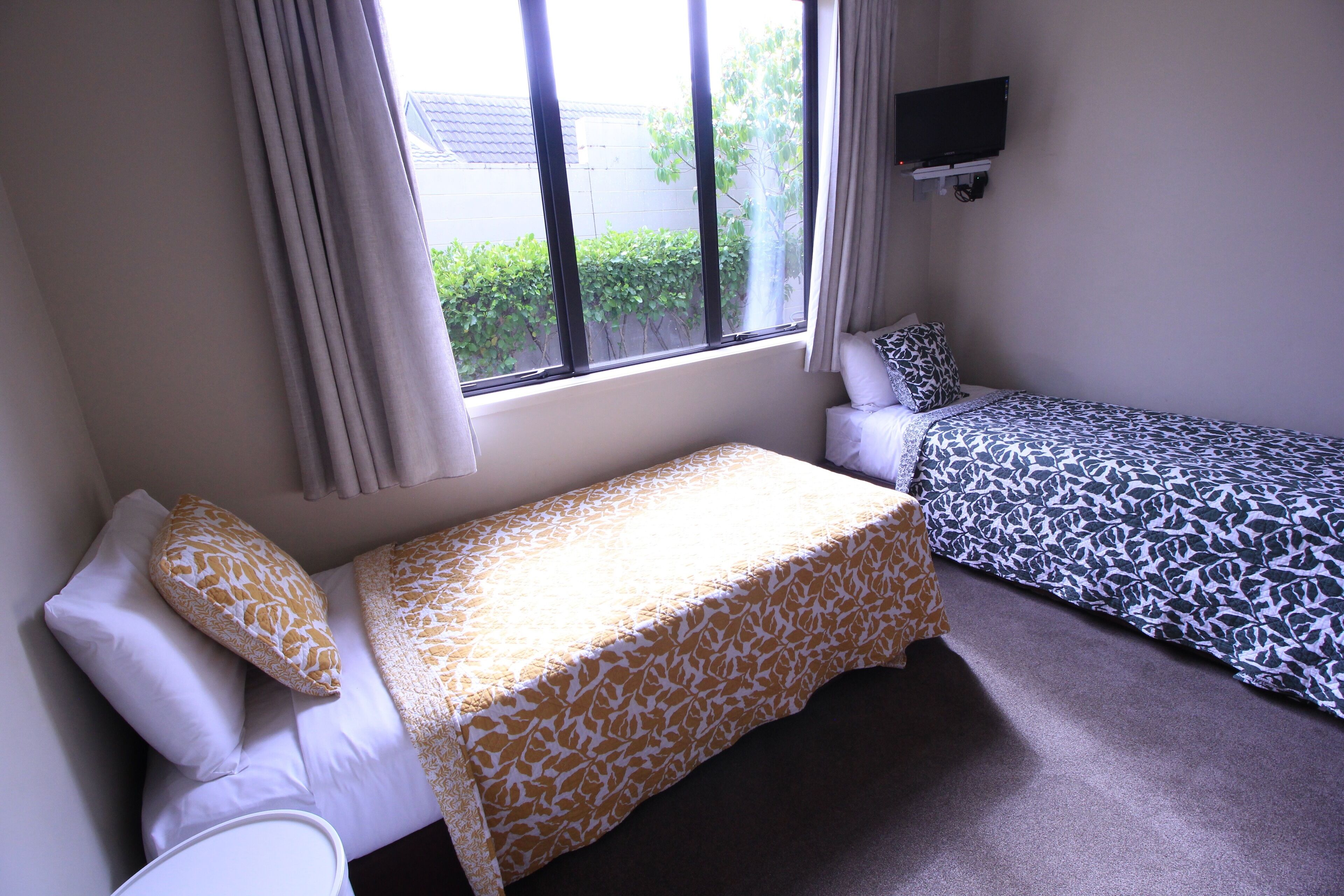 Quarto com uma cama de solteiro, um sofá e uma televisão presa na parede.